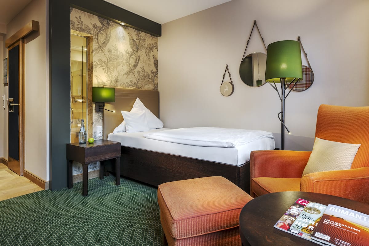 Quarto de hotel com uma cama, uma mesinha de centro com uma revista, uma cadeira e um abajur.