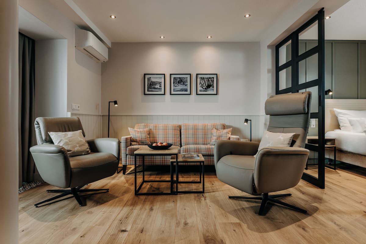 Uma sala de estar moderna com sofá, duas poltronas, uma mesa de centro e um aparador. Há três quadros pendurados na parede, uma luminária no teto e um aparelho de ar condicionado.