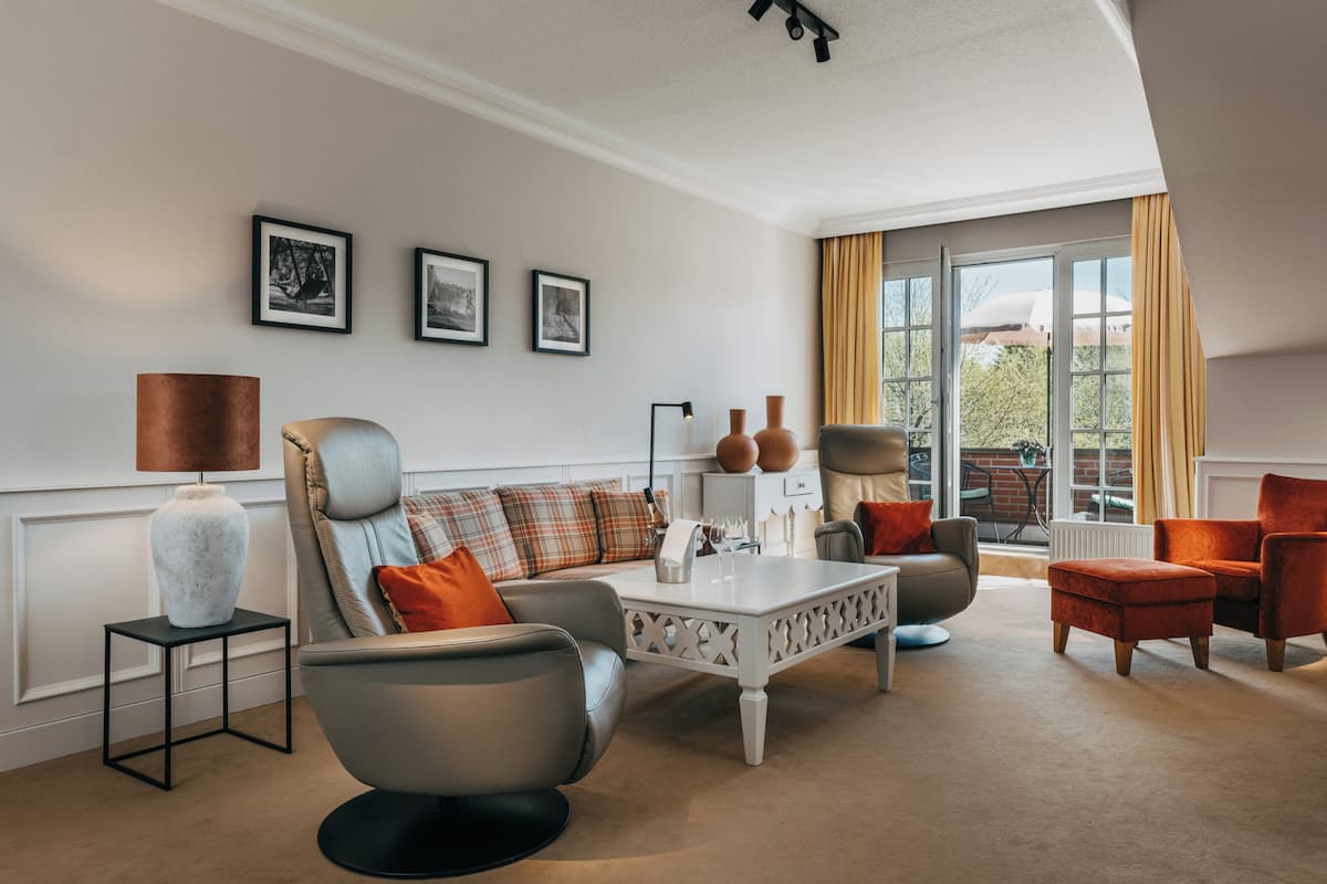 Uma sala de estar moderna com sofá, poltronas, mesa de centro e luminária. Há quadros nas paredes e uma janela com cortinas.