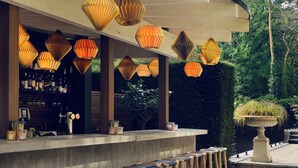 Uma área de bar com banquetas de madeira, lanternas de papel penduradas e um balcão de concreto.