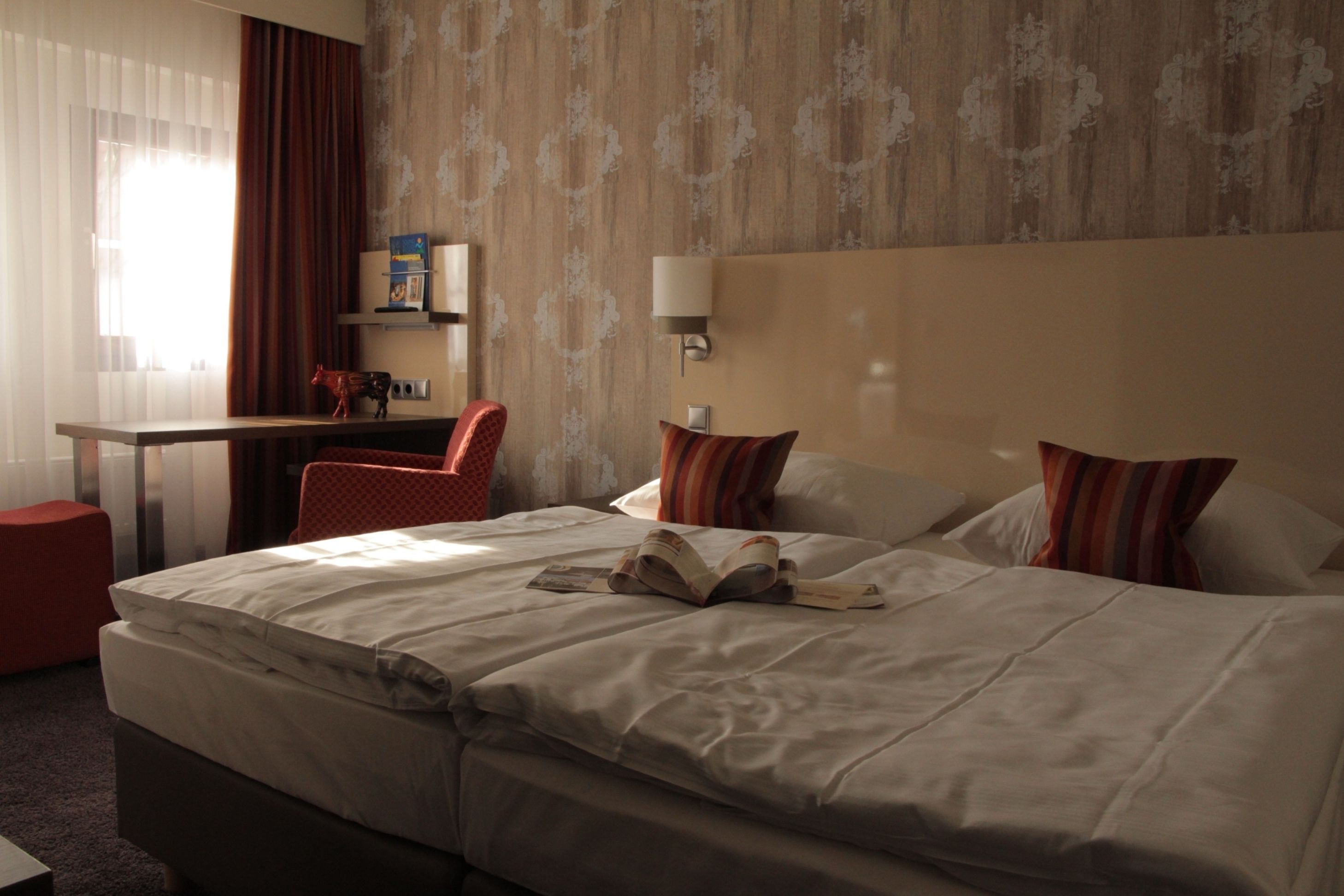 Quarto de hotel com uma cama grande, uma escrivaninha, uma cadeira e um abajur.