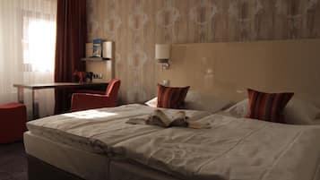 Quarto de hotel com uma cama grande, uma escrivaninha, uma cadeira e um abajur.