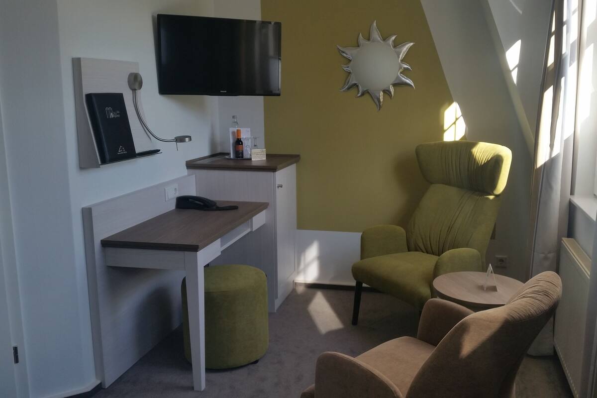 Quarto pequeno e moderno com uma escrivaninha, uma cadeira, um sofá, uma televisão e uma decoração de parede em formato de sol.