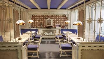 Uma sala de jantar com mobiliário branco ornamentado, cadeiras estofadas em roxo e painéis decorativos nas paredes.