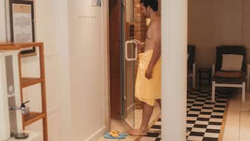 Um homem de toalha em pé numa porta, chão xadrez e um pilar branco.