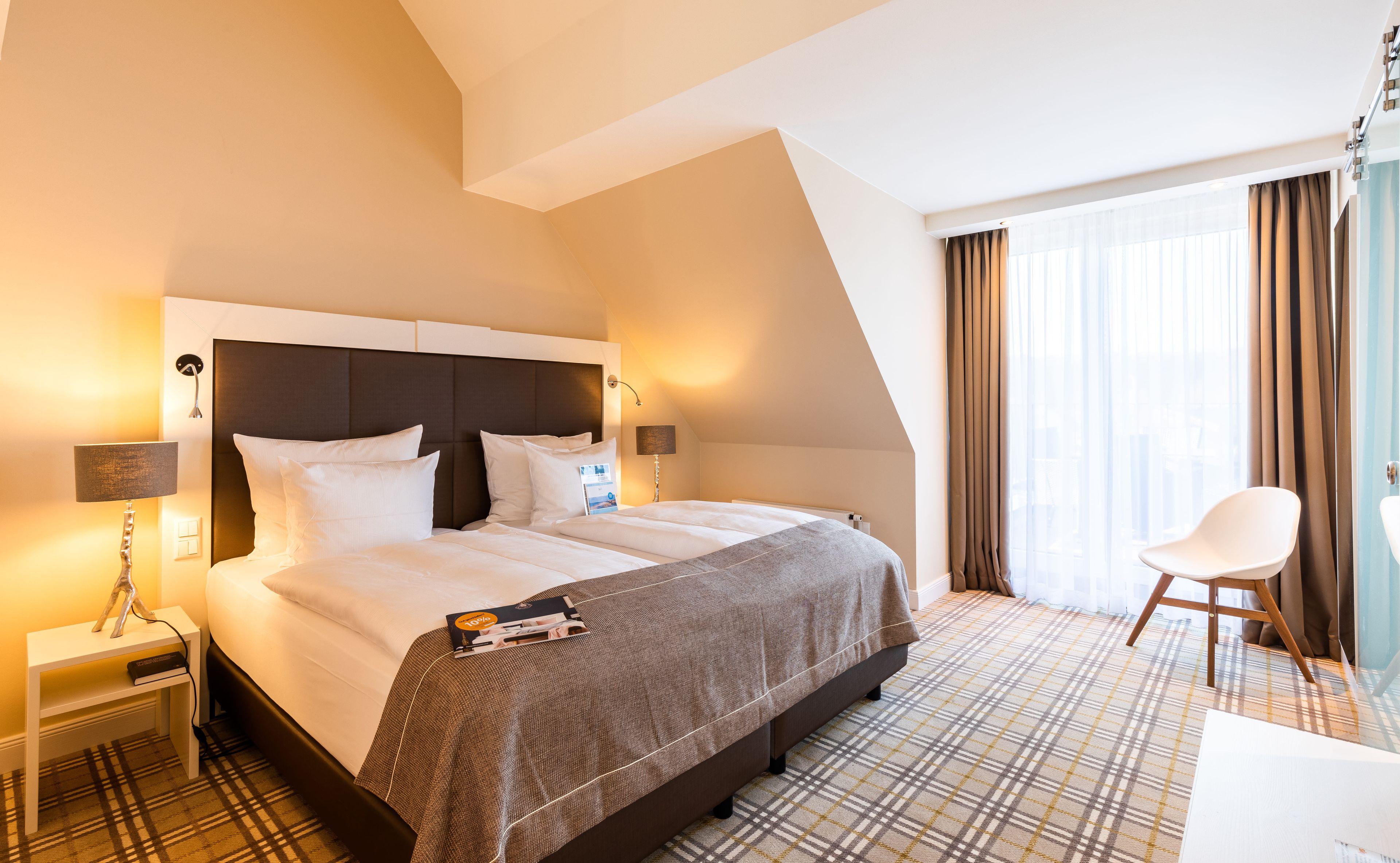 Quarto de hotel com cama grande, mesa de cabeceira, uma cadeira e vista para o exterior.