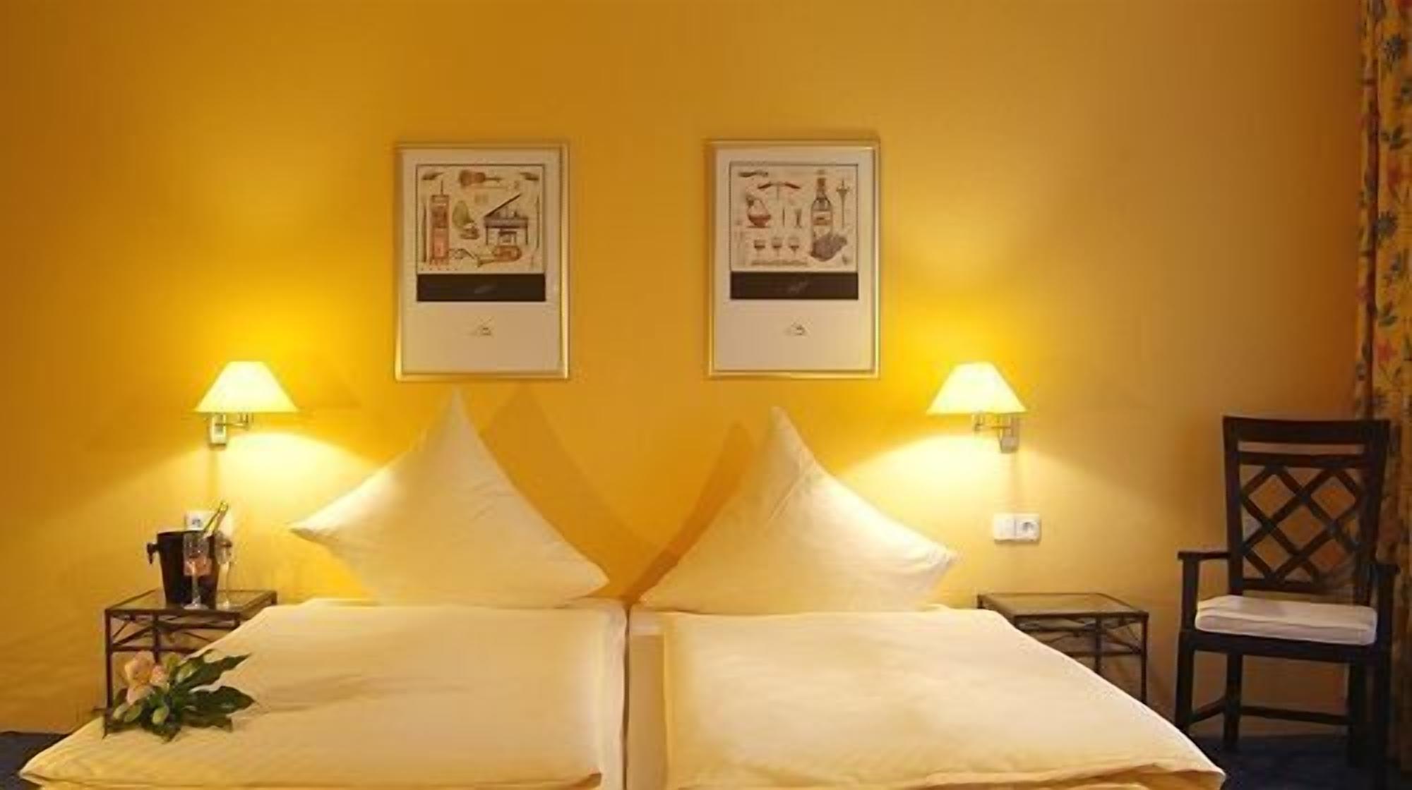 Quarto de hotel com cama de casal, duas mesas de cabeceira, duas luminárias e dois quadros na parede.