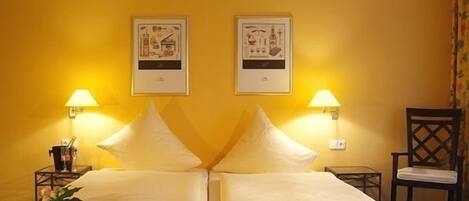 Quarto de hotel com cama de casal, duas mesas de cabeceira, duas luminárias e dois quadros na parede.