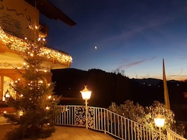 Um edifício com varanda, um pinheiro de Natal e céu noturno com a lua visível.