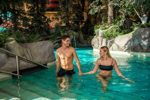 Um homem e uma mulher em uma piscina, cercados por pedras e vegetação.