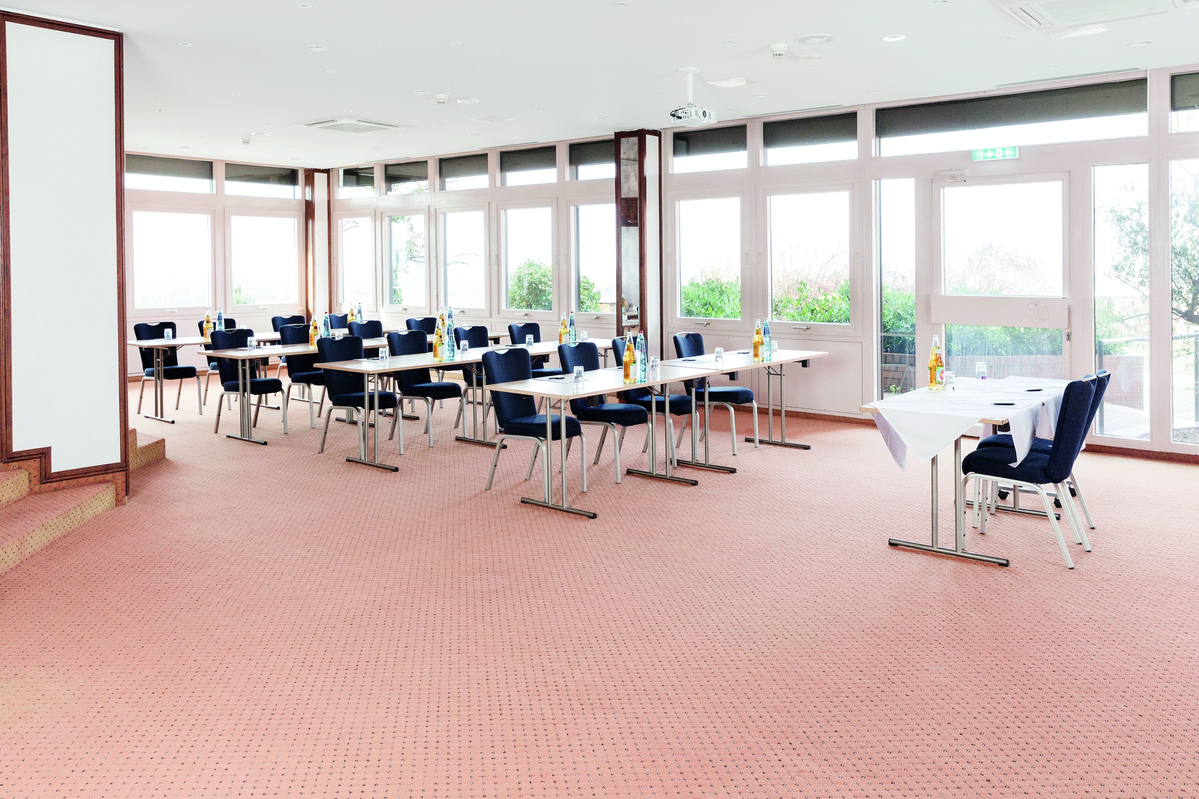Uma sala de conferências com mesas, cadeiras, amplas janelas e piso coberto por um tapete vermelho.