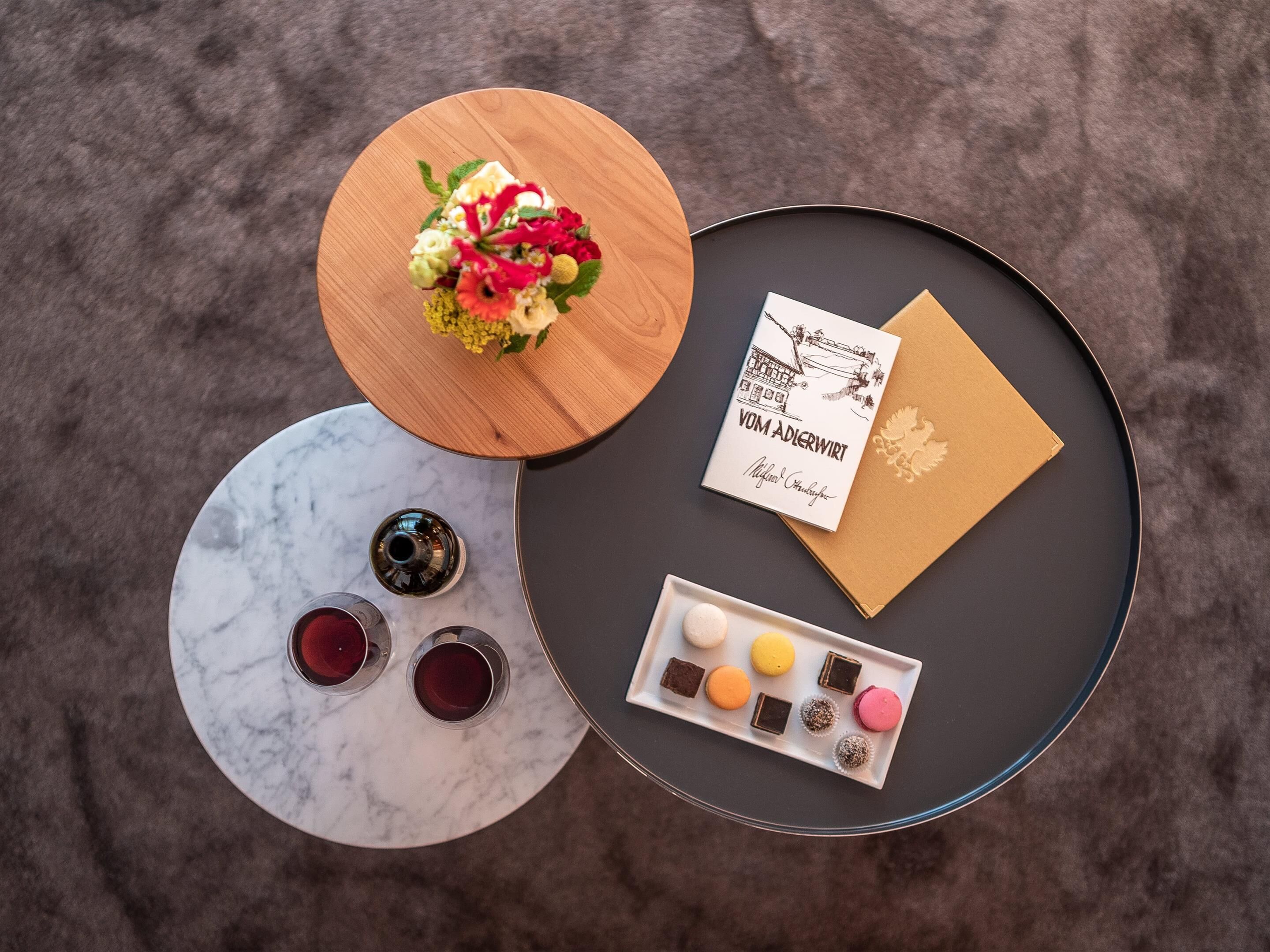 Uma mesa com um livro, um buquê de flores e uma bandeja de bombons variados.