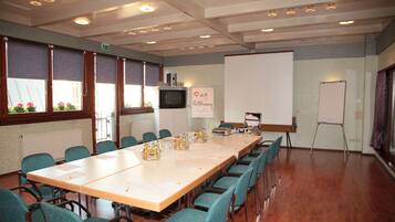 Uma sala de conferências com uma mesa comprida, cadeiras cor turquesa, um quadro branco e uma tela de projetor.