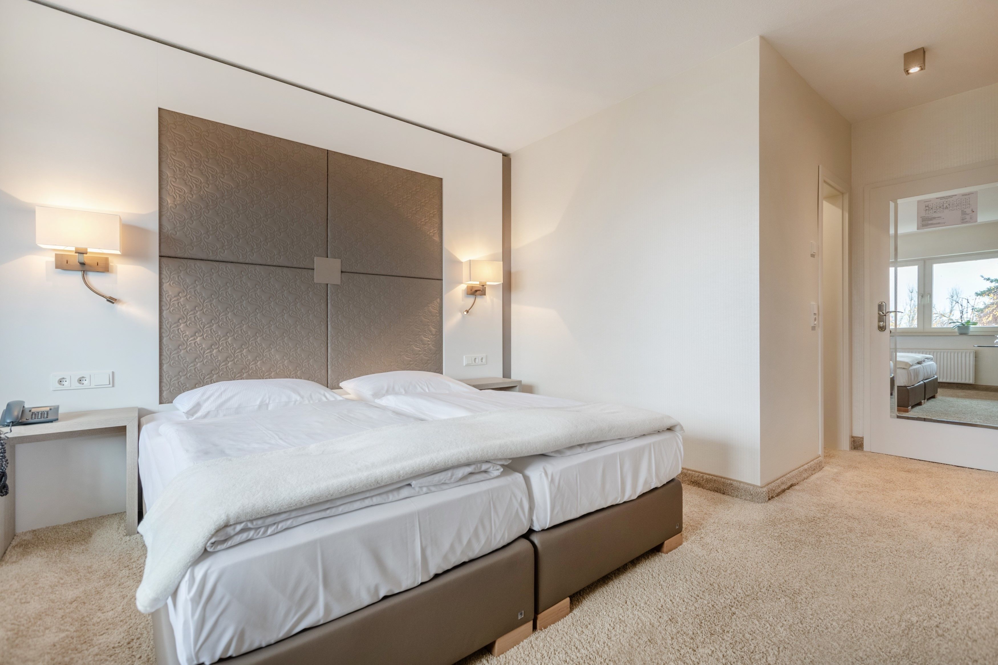 Quarto moderno com uma cama grande, duas mesas de cabeceira, luminárias fixadas na parede e um espelho grande.
