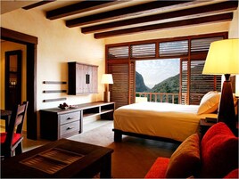Quarto com cama, escrivaninha, cadeira, armário e janela com vista para as montanhas.