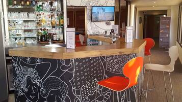 Uma área de bar com balcão, prateleiras cheias de garrafas, uma tela de televisão e duas cadeiras vermelhas.