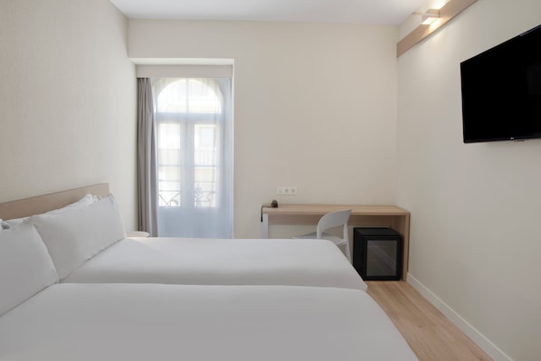 Quarto de hotel com duas camas, uma escrivaninha, uma cadeira, uma televisão e uma janela com cortinas.