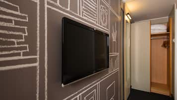 Quarto com televisão de tela plana na parede, guarda-roupa de madeira e piso coberto por carpete.