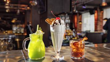 Três bebidas sobre um balcão de bar com fundo desfocado.
