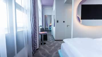 Quarto de hotel com cama, escrivaninha, cadeira e televisão fixada na parede.