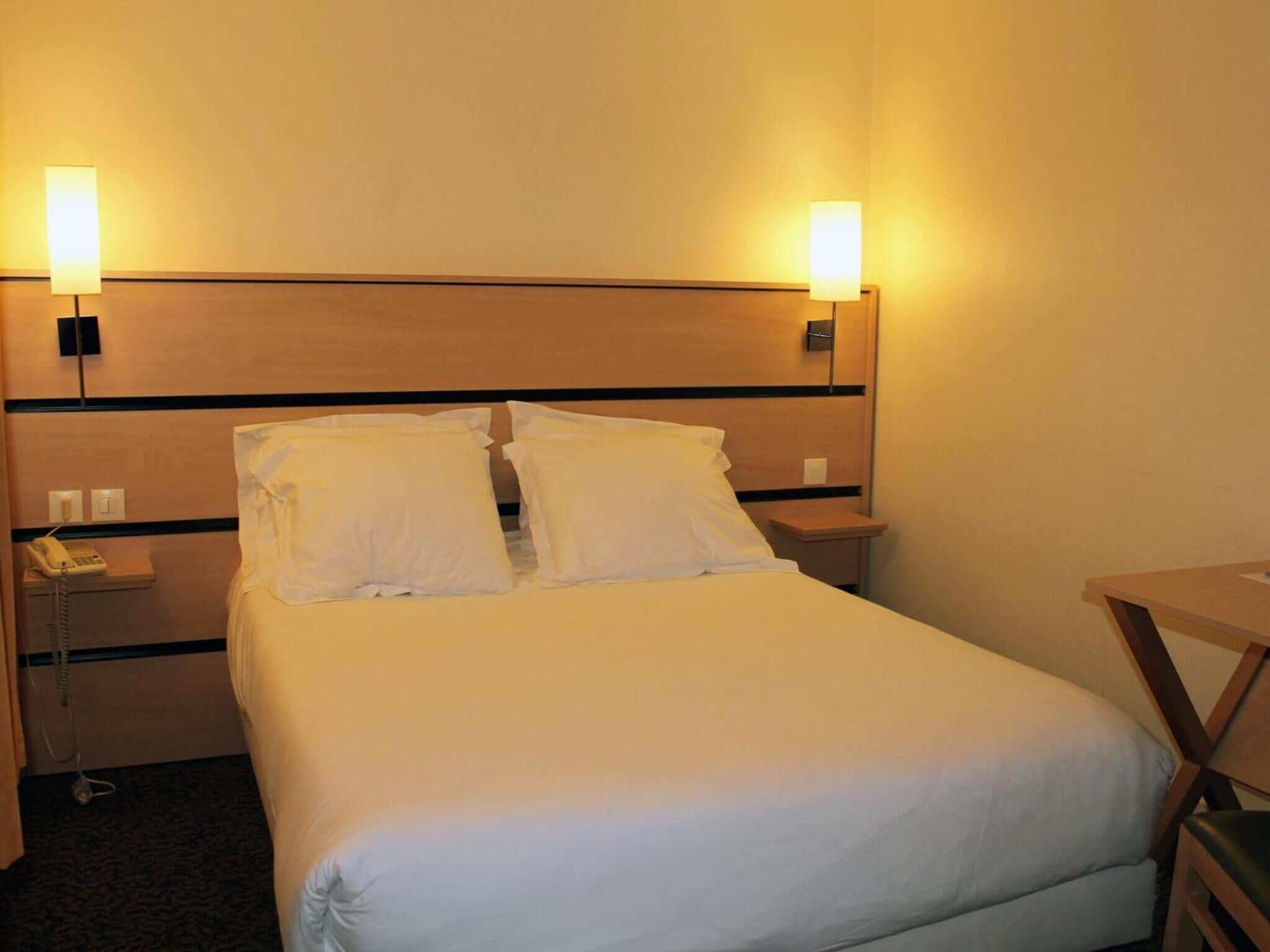 Quarto de hotel com uma cama grande, duas mesas de cabeceira e uma luminária em cada lado.