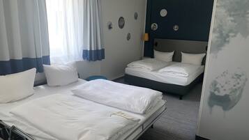 Quarto de hotel com uma cama de casal, uma cama individual, uma mesinha de cabeceira, uma luminária e uma parede com decorações circulares.