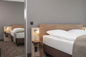 Quarto de hotel com uma cama, mesas de cabeceira e luminárias fixadas na parede.