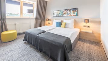 Quarto de hotel com duas camas, uma janela com cortinas, um banquinho amarelo e um quadro na parede.