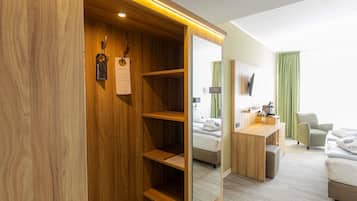 Quarto de hotel com armário de madeira, escrivaninha com cadeira, cama, televisão e espelho.
