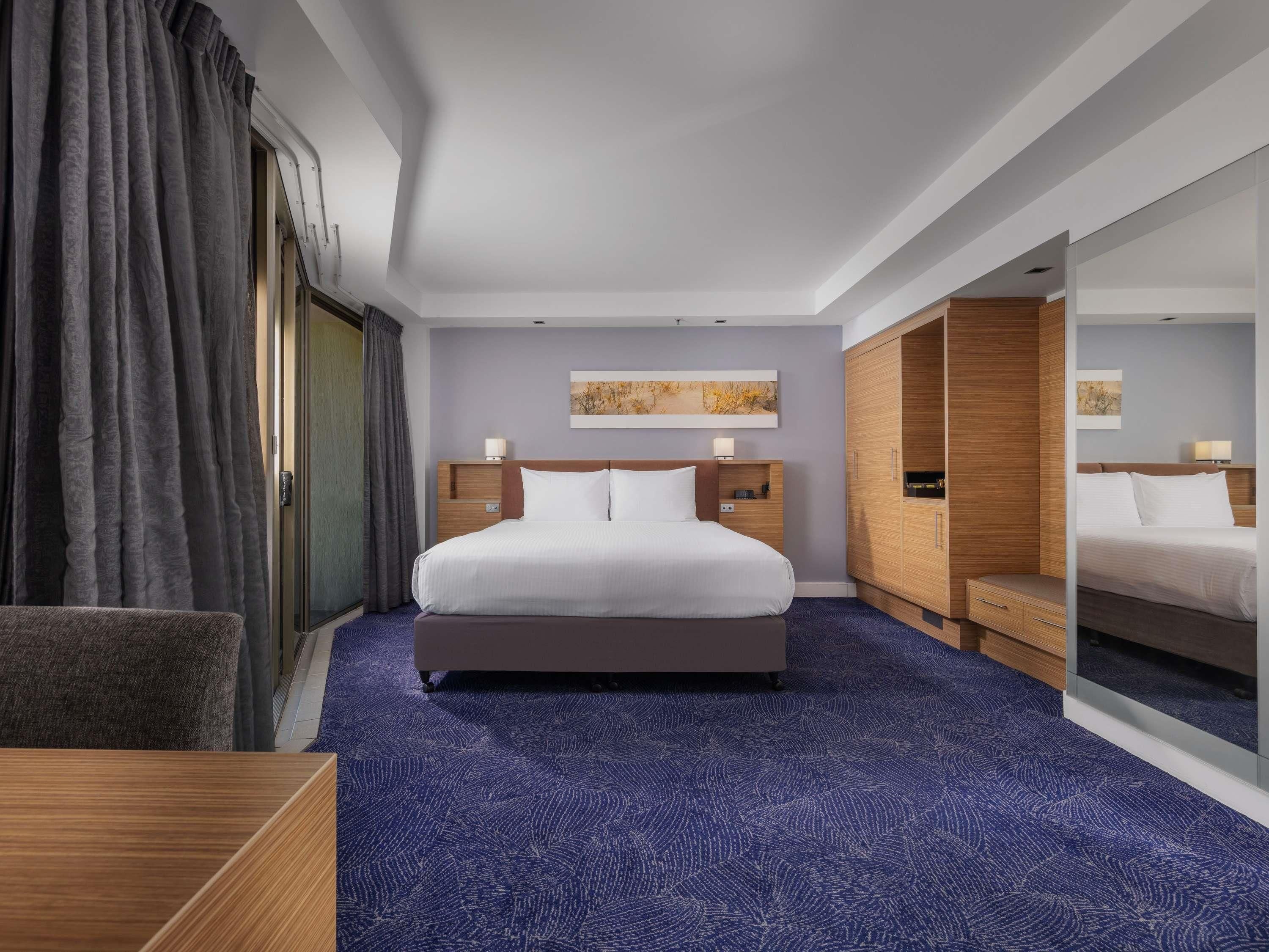 Quarto de hotel com uma cama grande, mesa de cabeceira, guarda-roupa e espelho.