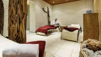 Uma sala de spa com duas camas, decoração em madeira e uma parede de tijolos brancos.