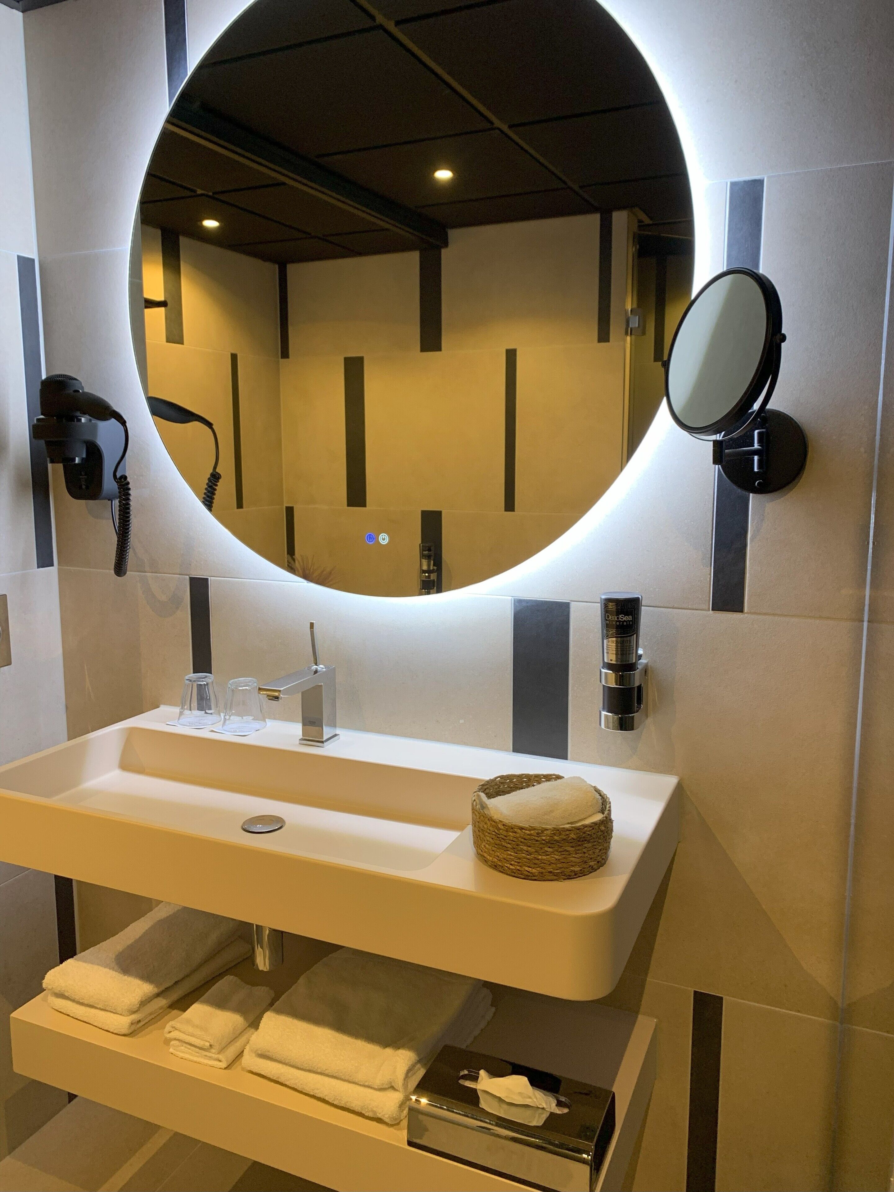 Uma casa de banho moderna com um espelho redondo, lavatório e porta-toalhas.