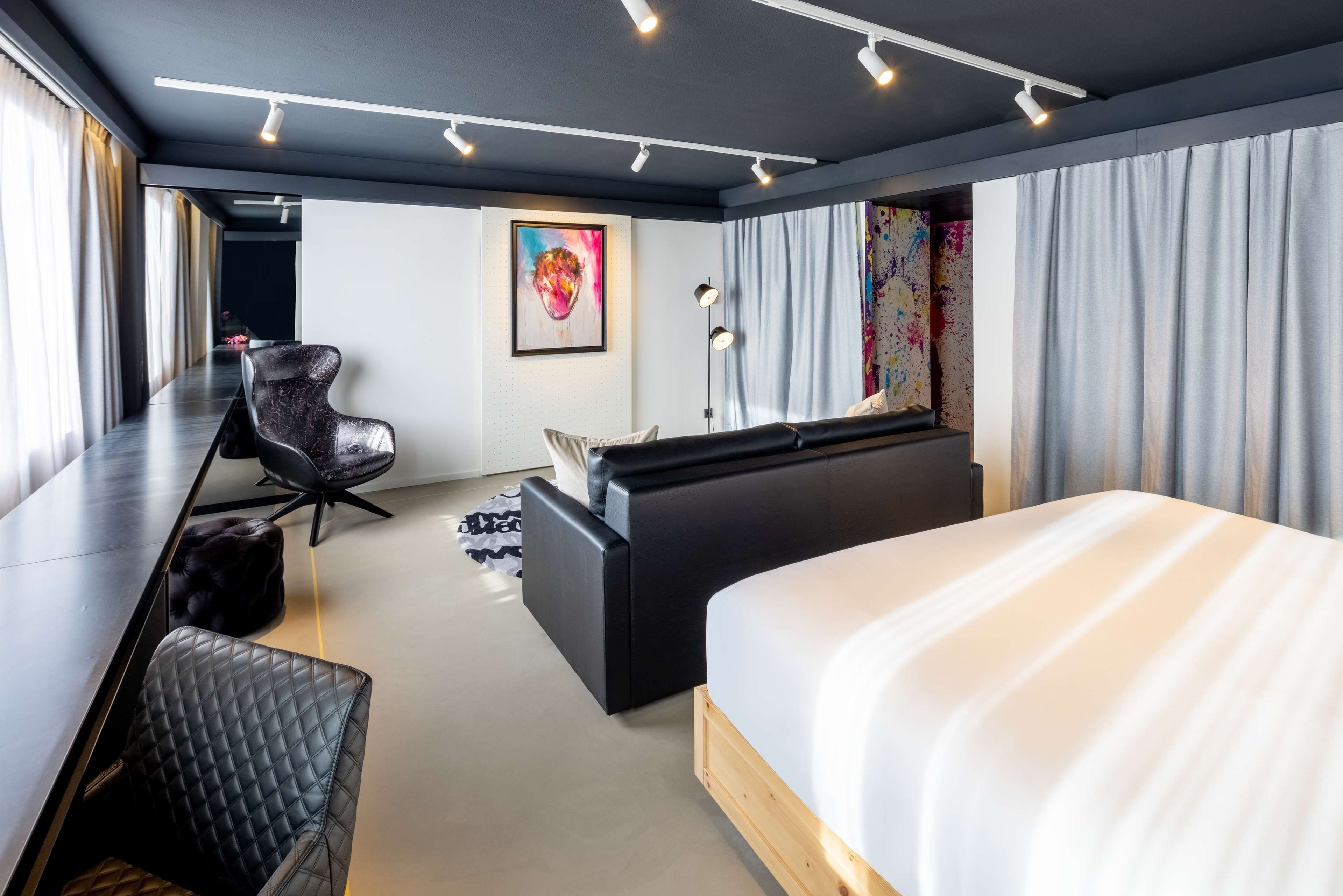 Quarto de hotel moderno com uma cama grande, uma escrivaninha, uma cadeira e um sofá.