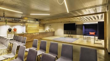 Uma sala de conferências com uma mesa comprida, várias cadeiras, um palco e uma tela grande.