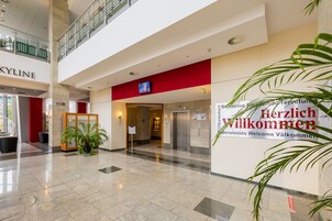 Um hall de hotel moderno, com esquema de cores vermelho e branco, um balcão de recepção e uma placa dando as boas-vindas aos hóspedes.