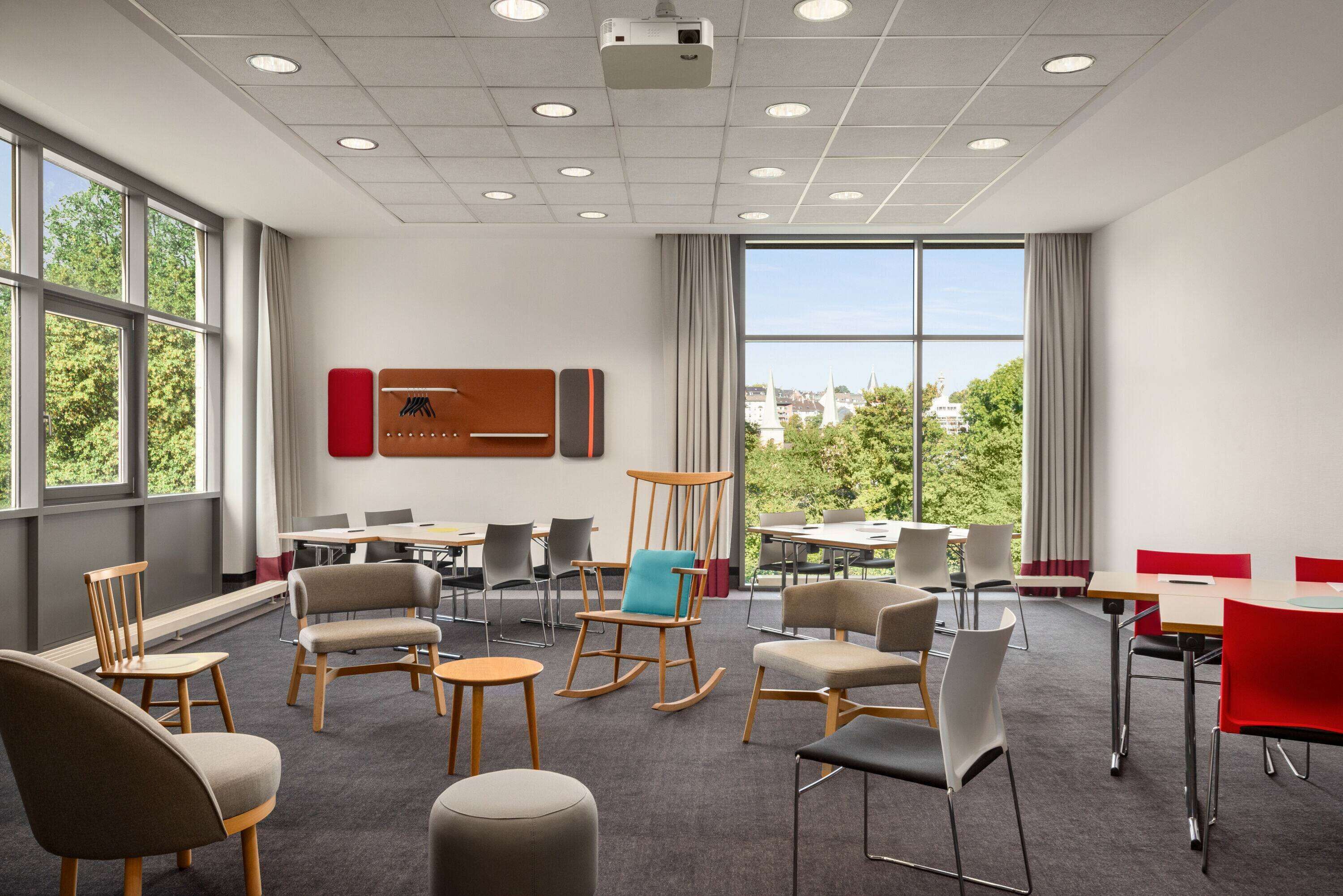 Uma sala de conferências moderna com uma janela grande, diversas opções de assento e um projetor no teto.