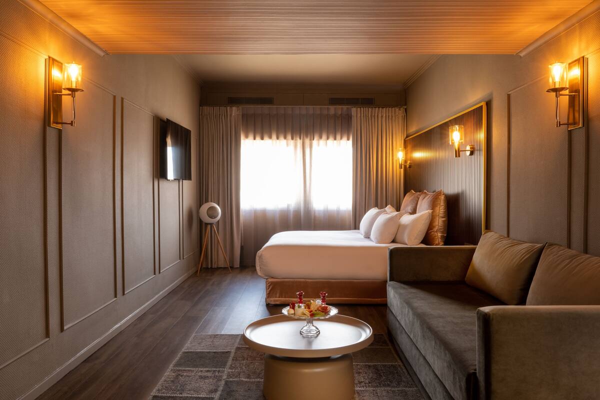 Quarto de hotel com cama, sofá, mesa de centro e arandelas na parede.