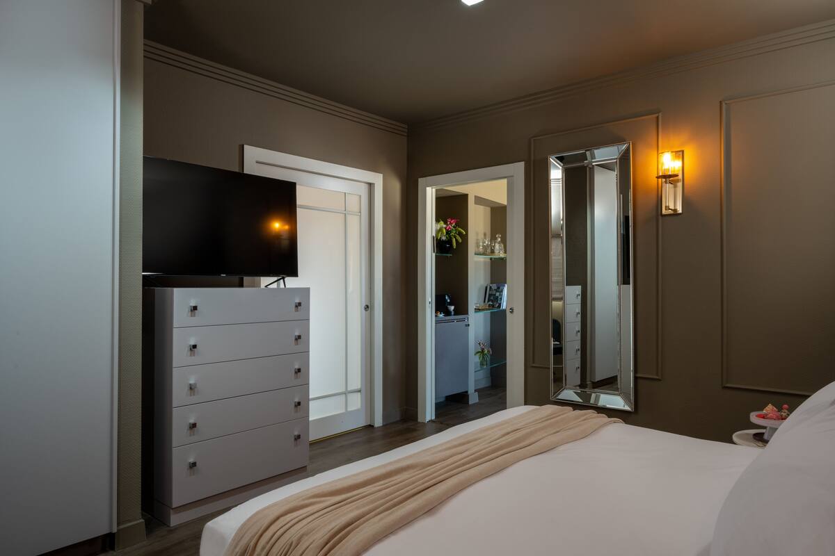 Quarto de hotel com cama, penteadeira, televisão, espelho e banheiro visível por uma porta aberta.