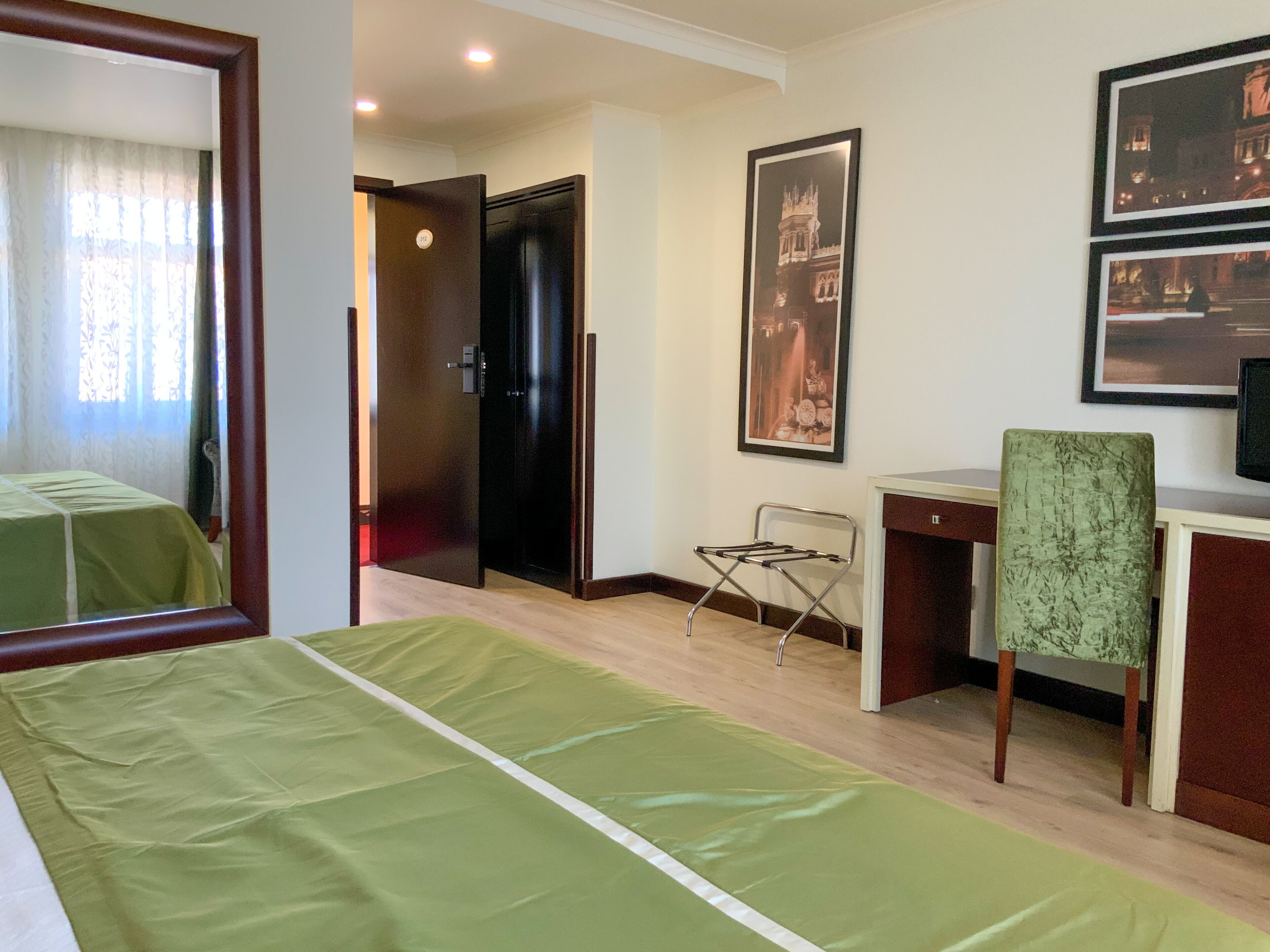 Quarto de hotel com cama, escrivaninha, cadeira e espelho.
