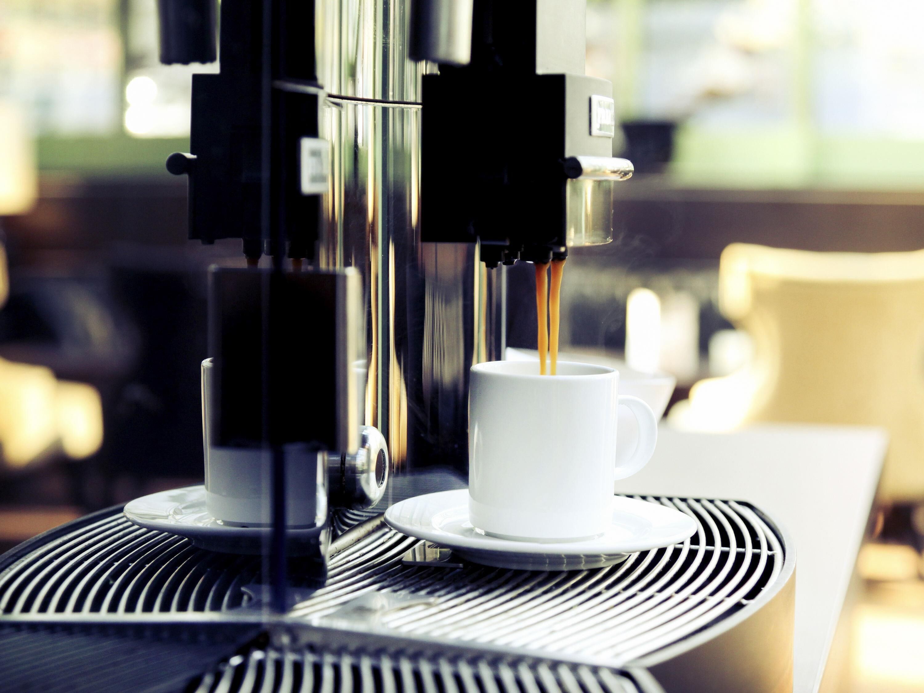 Máquina de café a servir expresso numa chávena sobre uma mesa com apoio de copos a preto e branco.