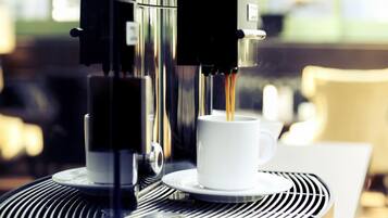 Máquina de café a servir expresso numa chávena sobre uma mesa com apoio de copos a preto e branco.