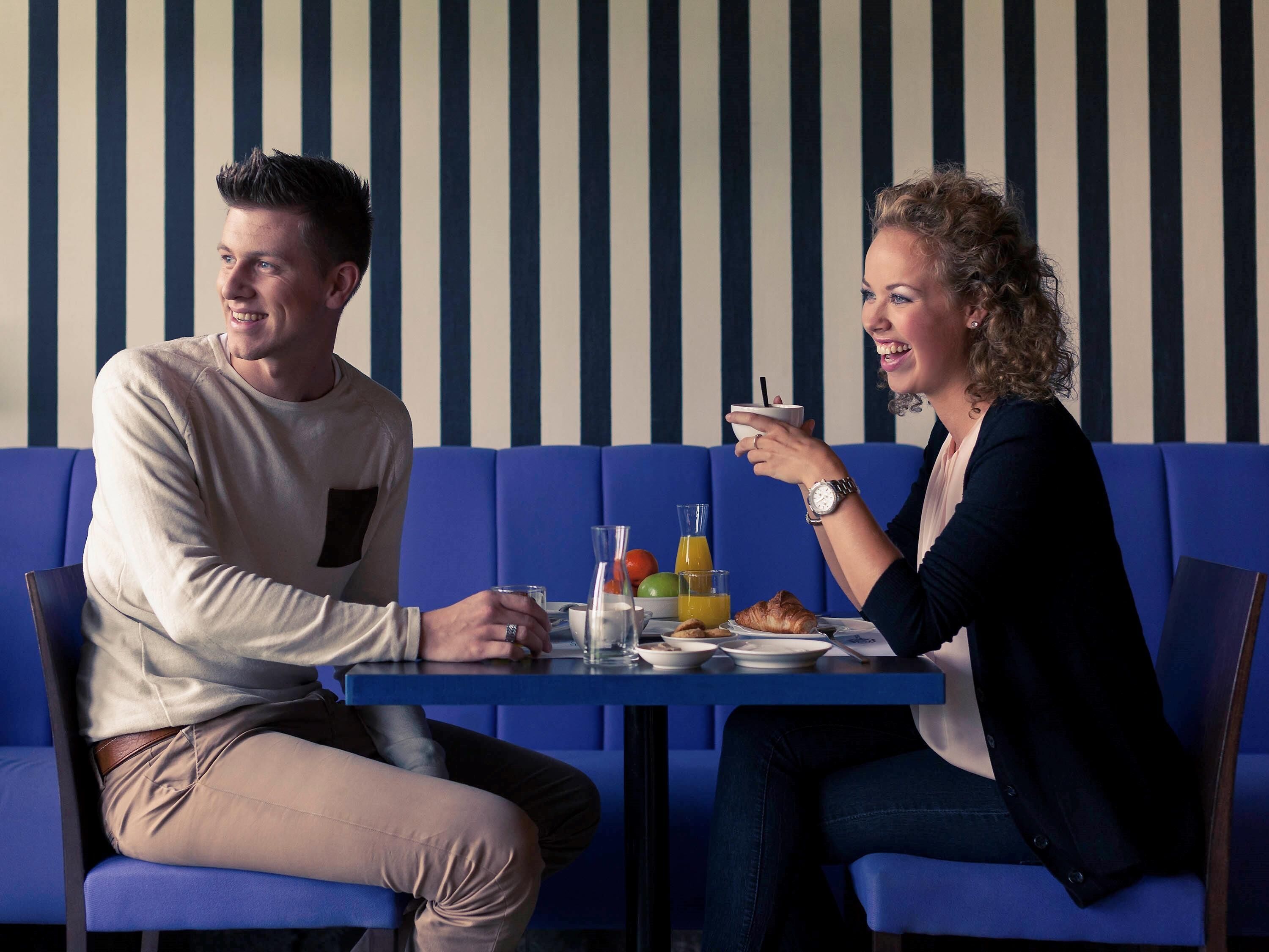 Uma área de refeições com um sofá azul e uma mesa posta com pratos, copos e um croissant.