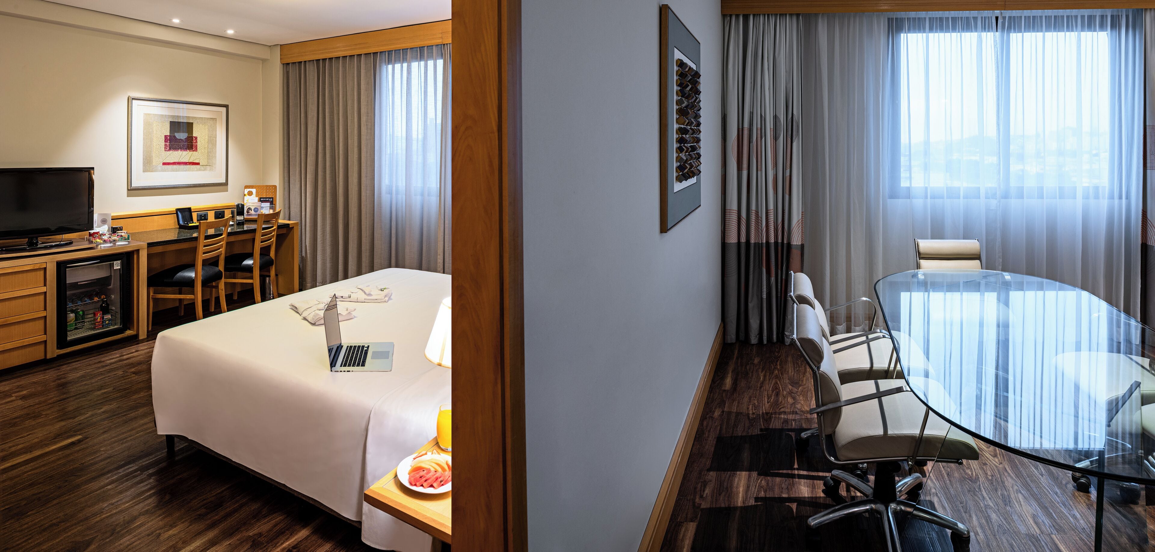 Quarto de hotel com cama, escrivaninha, cadeira, televisão e mesa de jantar com cadeiras.