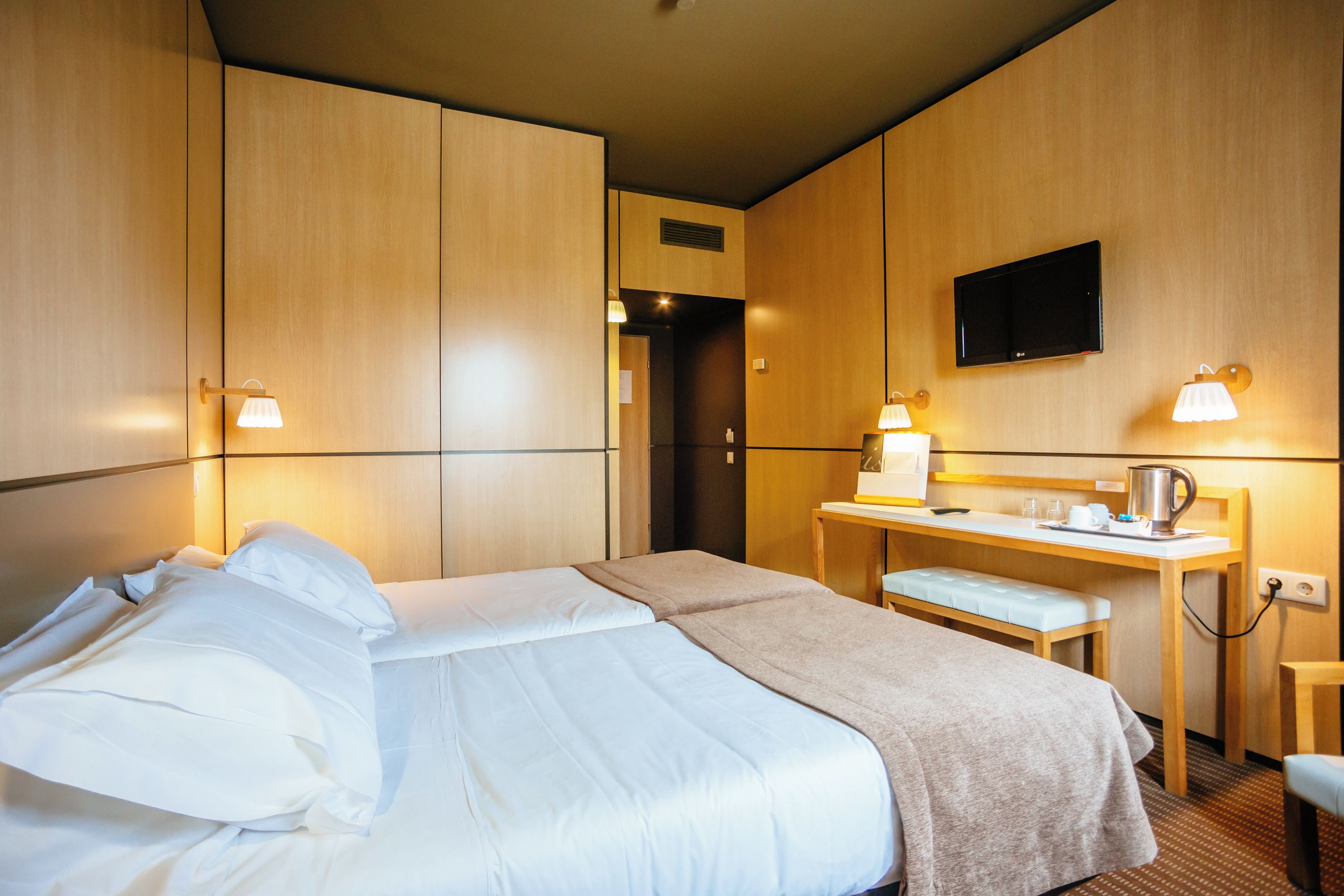 Quarto de hotel com duas camas, uma escrivaninha, televisão e máquina de café.
