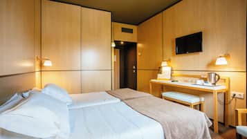 Quarto de hotel com duas camas, uma escrivaninha, televisão e máquina de café.