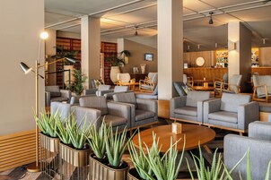 Uma área de estar moderna com sofás e poltronas, uma mesa de centro de madeira e plantas de aloe em vasos.