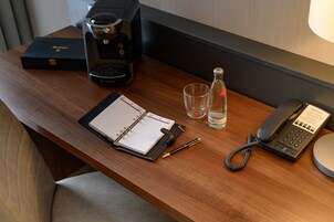 Uma mesa de madeira com um caderno, caneta, máquina de café, garrafa de água, copo e telefone.