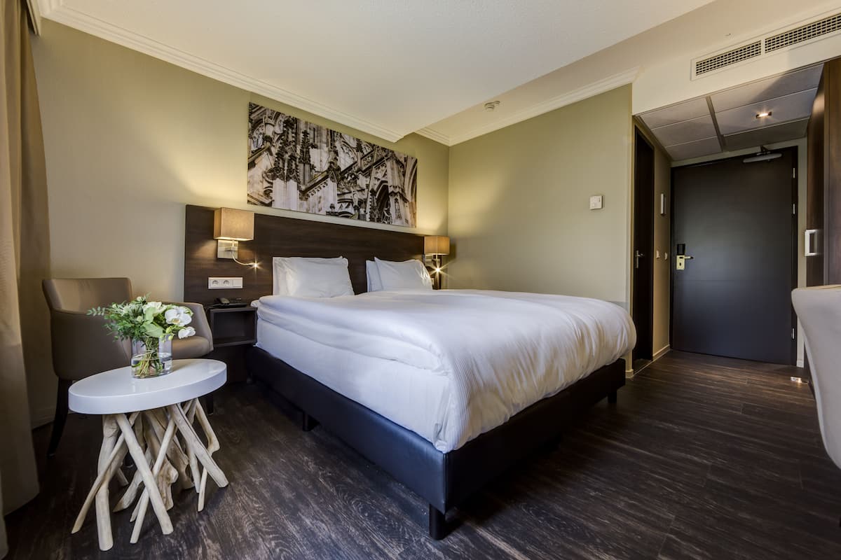 Quarto de hotel com uma cama grande, mesas de cabeceira, uma obra de arte pendurada na parede e uma porta que dá para outro quarto.