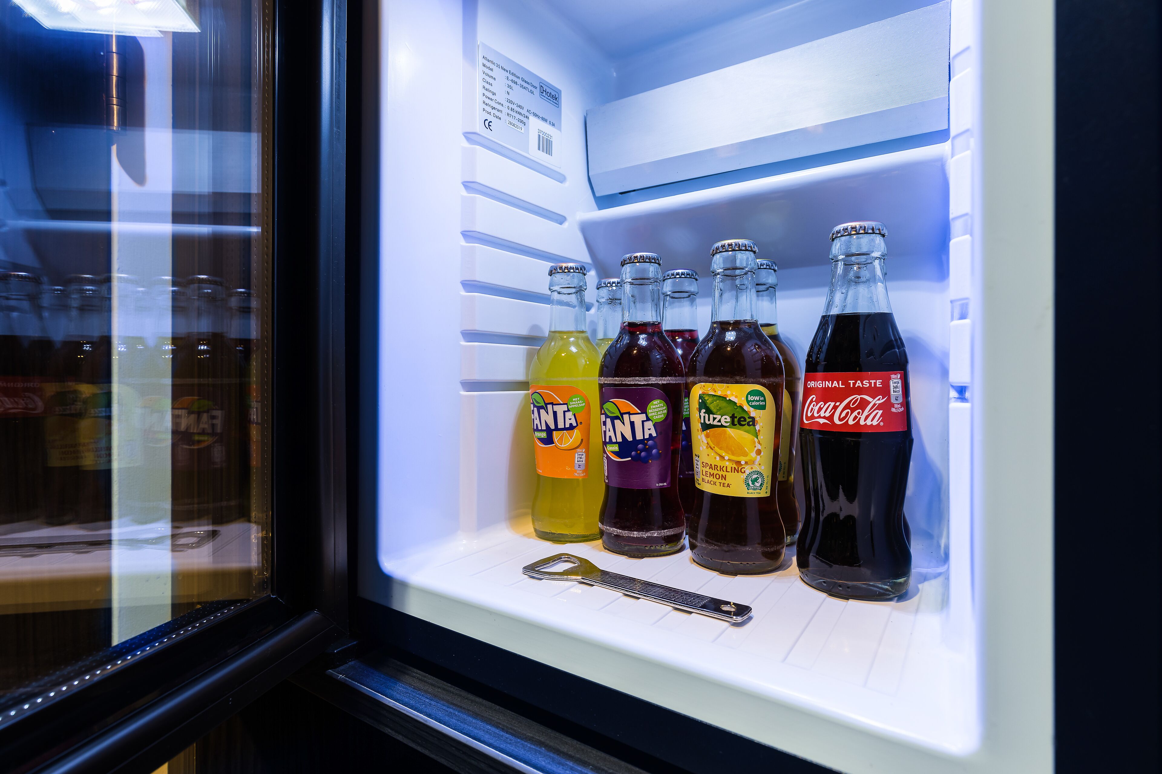 Uma geladeira com várias garrafas de bebidas, incluindo Fanta, FuzeTea e Coca-Cola.