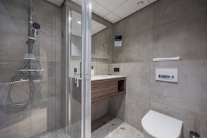Um banheiro moderno com chuveiro em cabine de vidro, toucador de madeira e vaso sanitário branco.